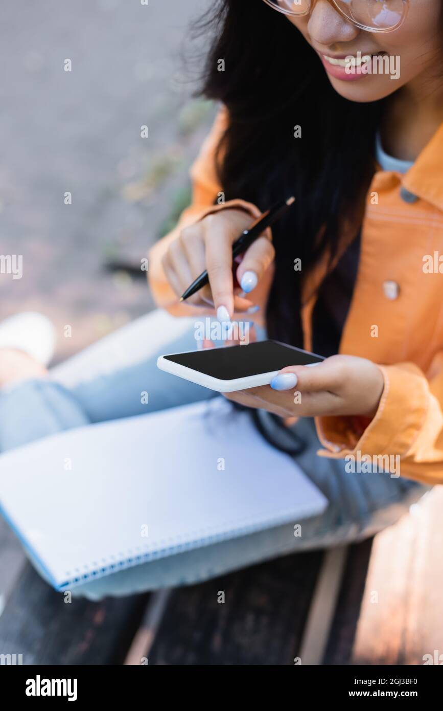 partial view of smiling woman using mobile phone with blank screen ...