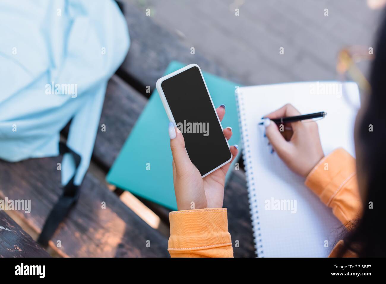 partial view of student writing in notebook while holding smartphone ...