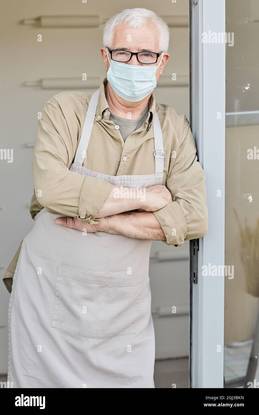 Portrait of aged Caucasian baker in apron and facial mask leaning on ...
