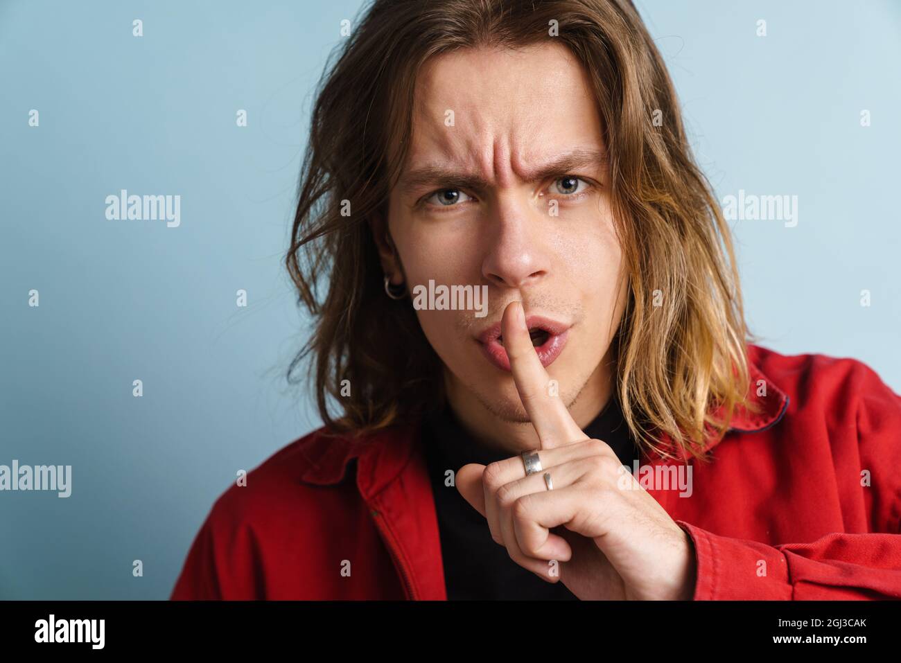 Young white man frowning while showing silence gesture at camera ...