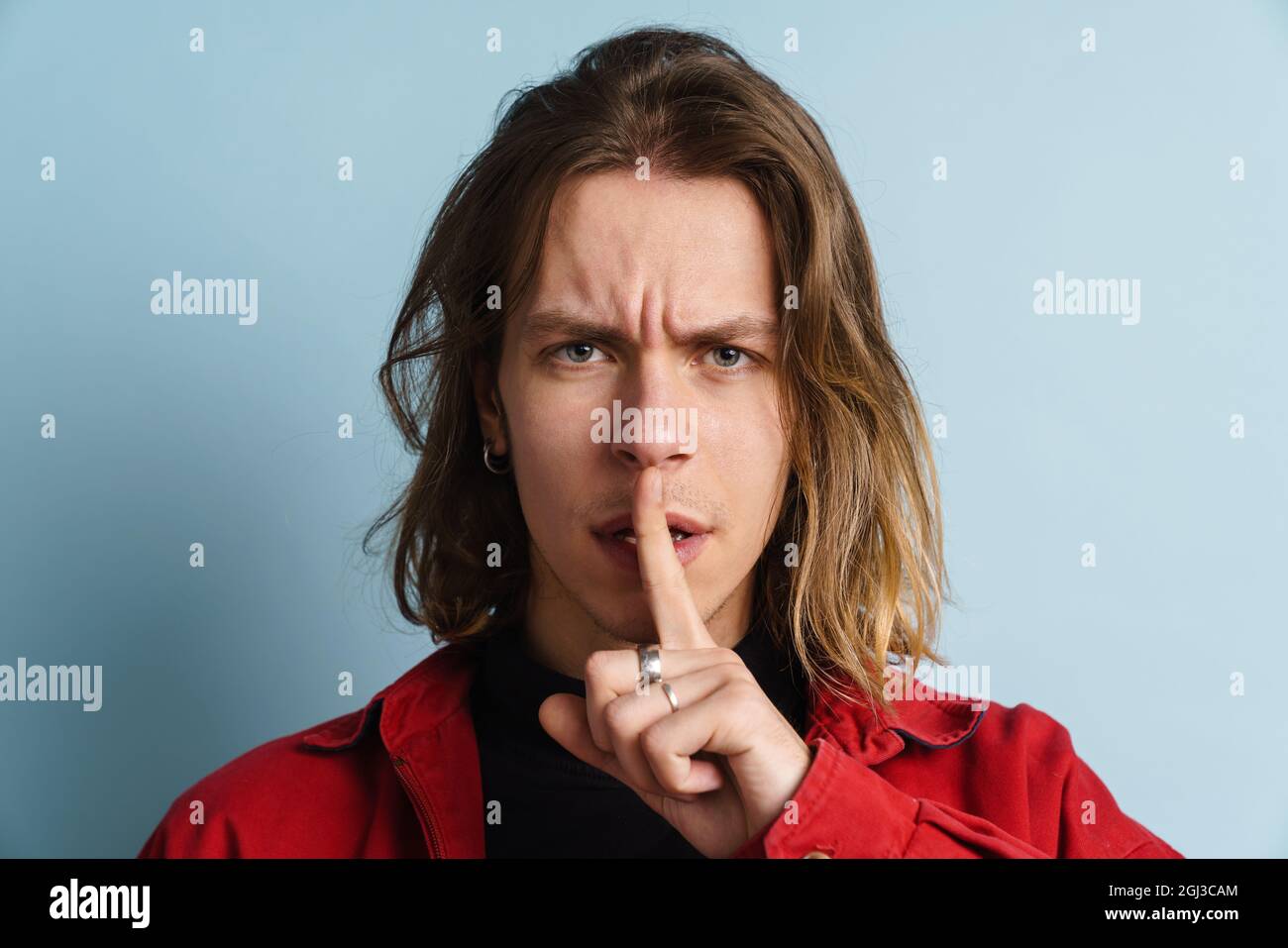 Young white man frowning while showing silence gesture at camera ...