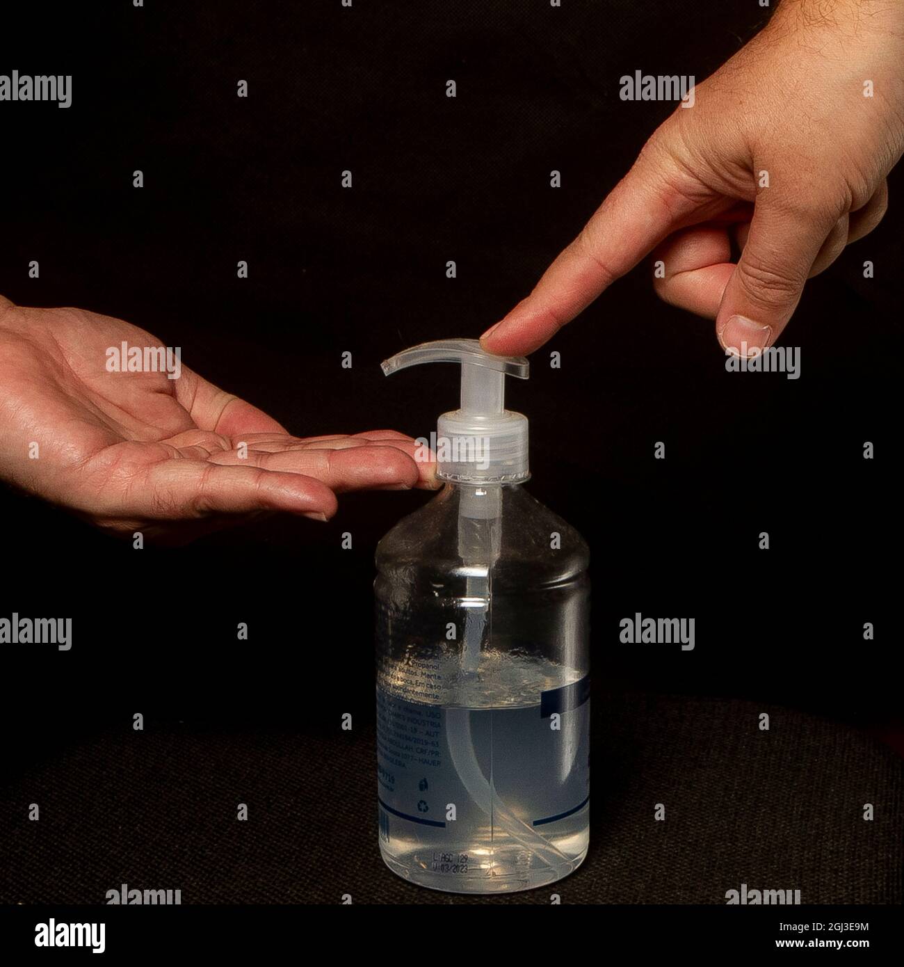 On a black background, male hand opens a container with alcohol gel to ...