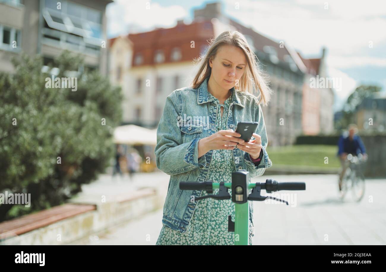 Woman using app on smartphone to unlock electric scooter on the street ...