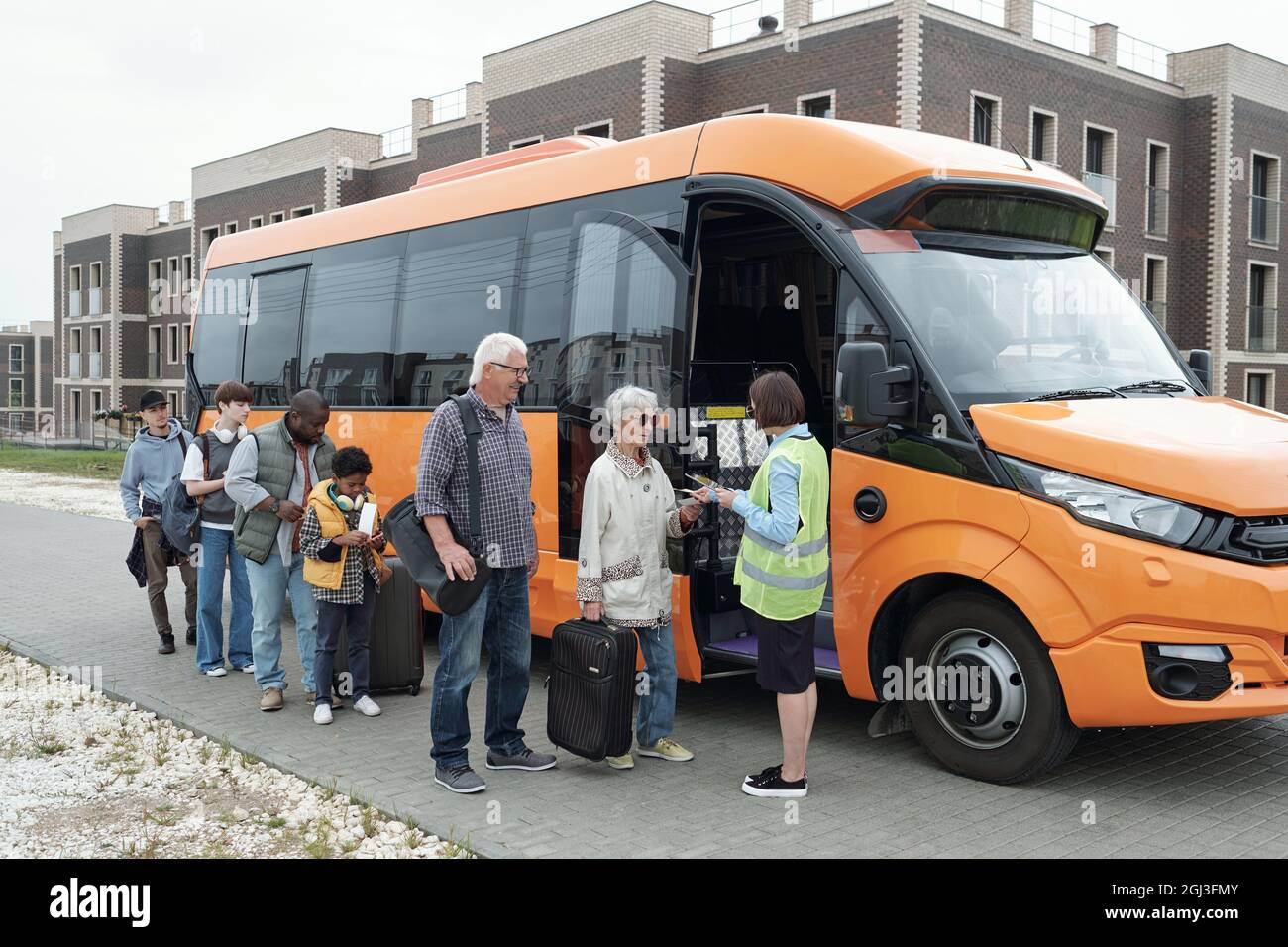 Female transportation supervisor in green vest standing at open bus ...