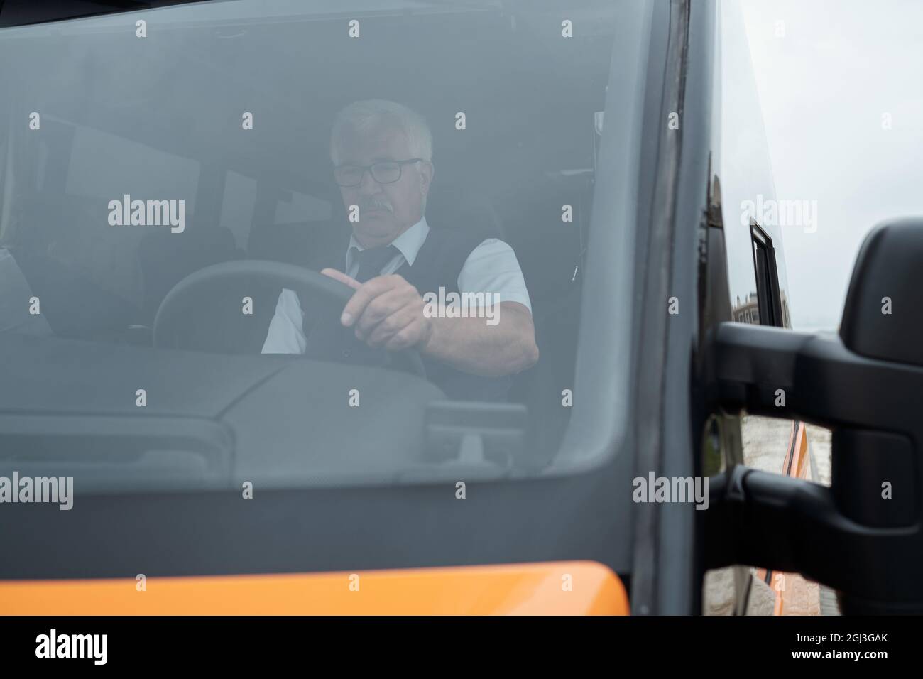 Behind windshield view of serious aged Caucasian bus driver in glasses ...