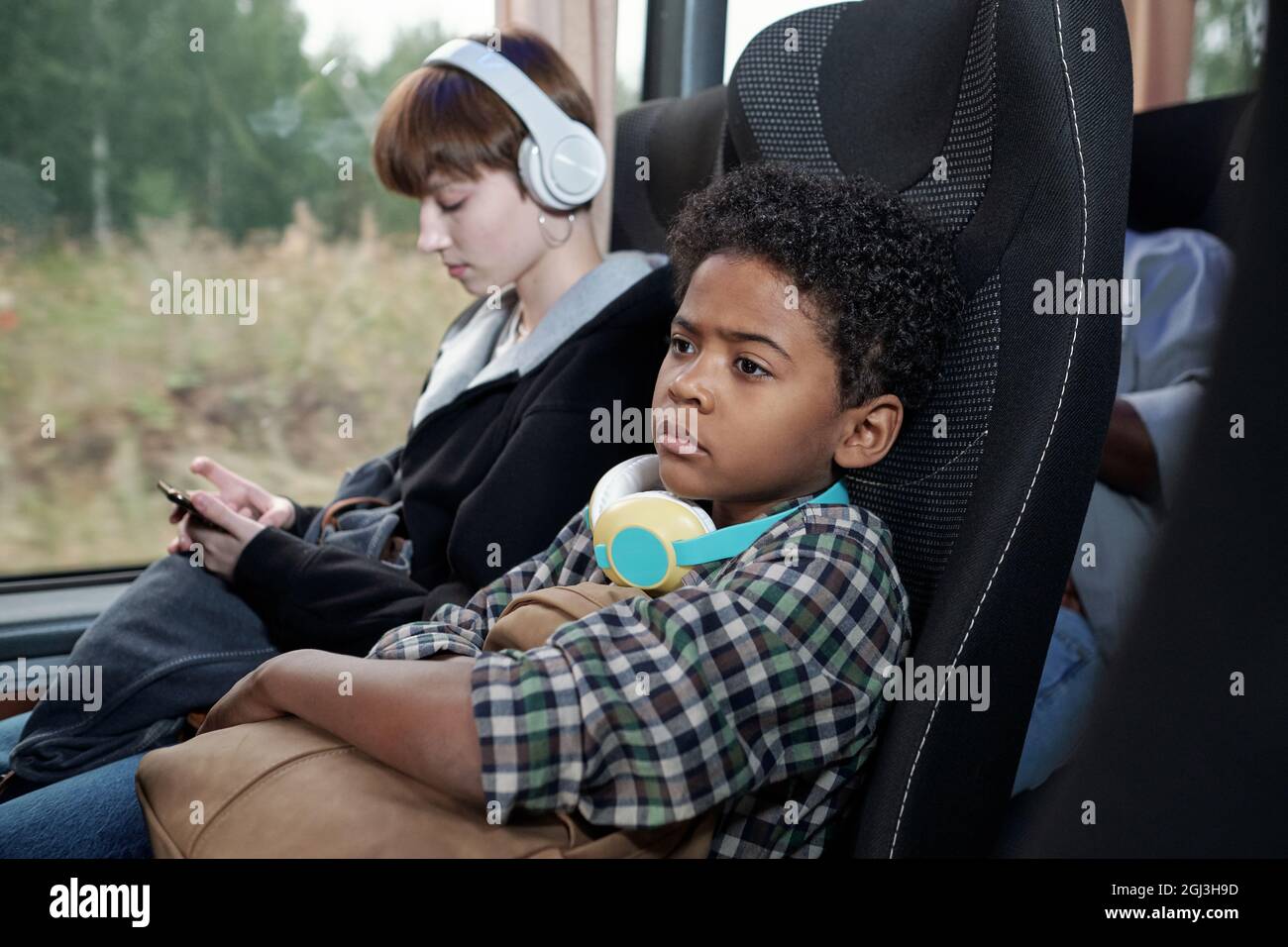 Serious tired black boy with curly hair embracing bag while riding bus ...