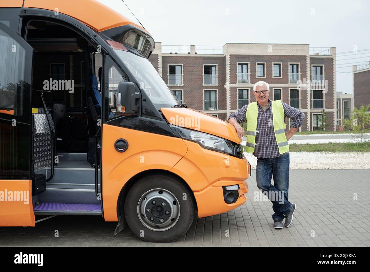 Smiling aged Caucasian bus driver in eyeglasses and green vest leaning ...