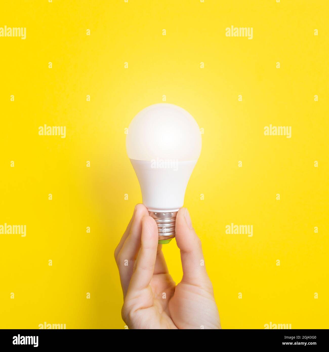 Hand holding a LED light bulb on bright yellow background. Using ...