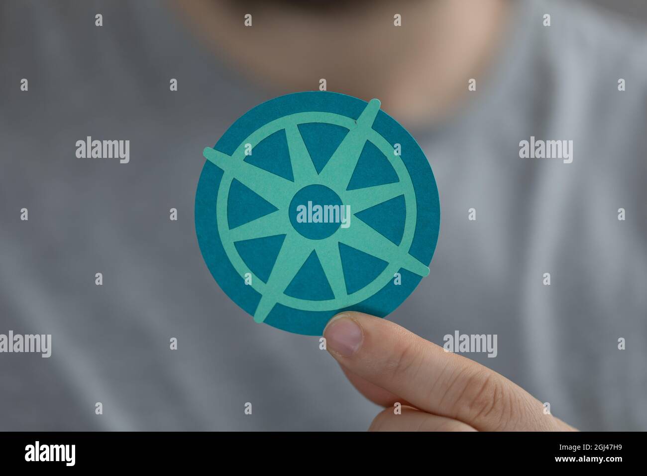 Closeup of a man holding a small blue paper cutout of a compass in his ...