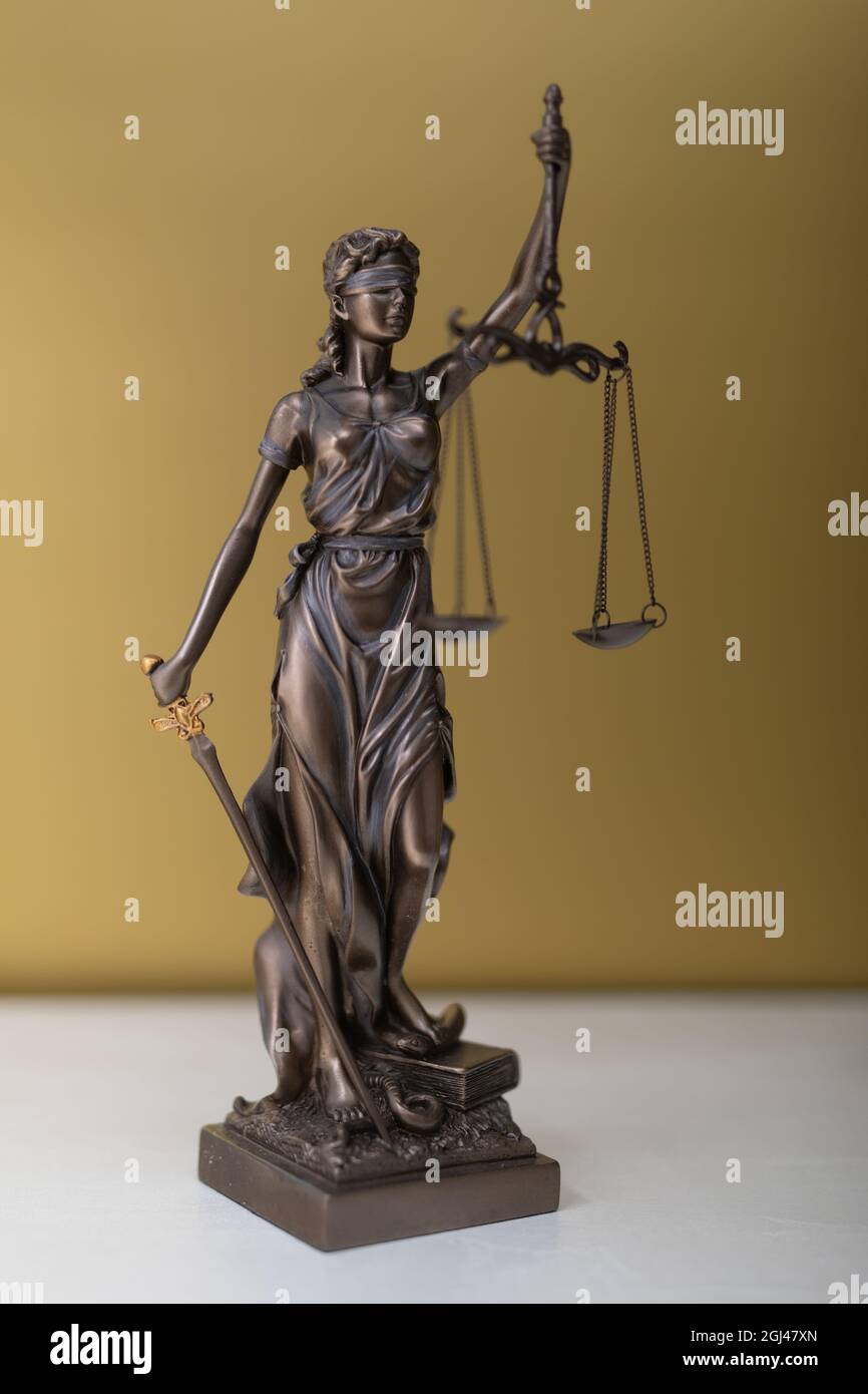 Vertical shot of a small bronze statue of a woman holding scales with a ...