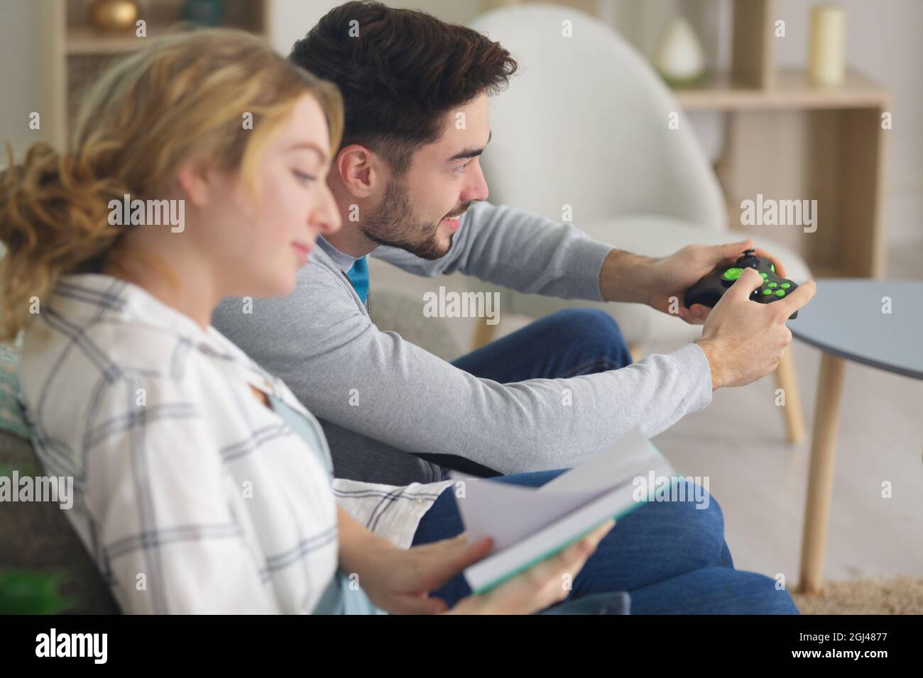 boyfriend playing console partner reading Stock Photo - Alamy