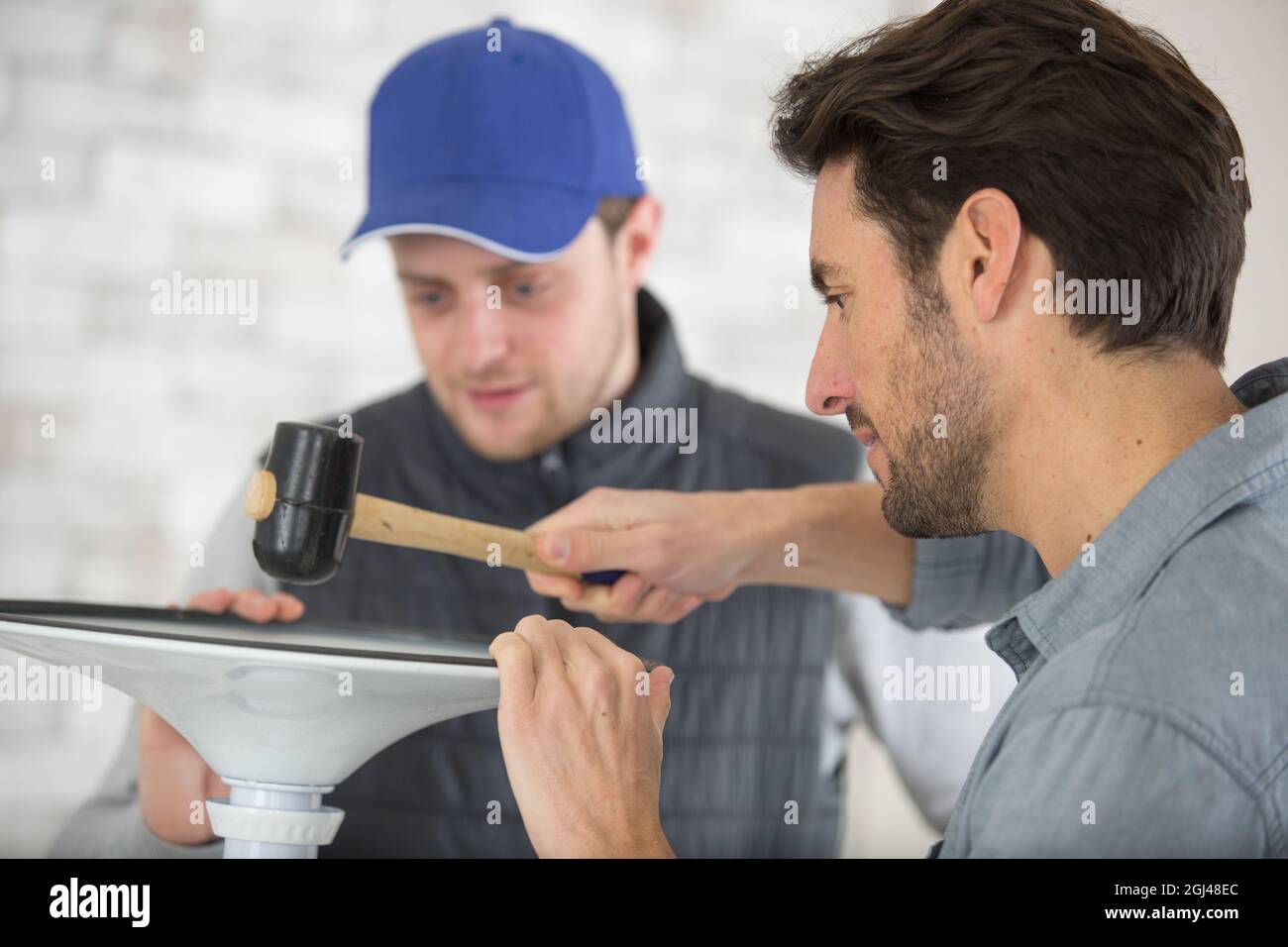 two men are using a hammer on a beach Stock Photo - Alamy