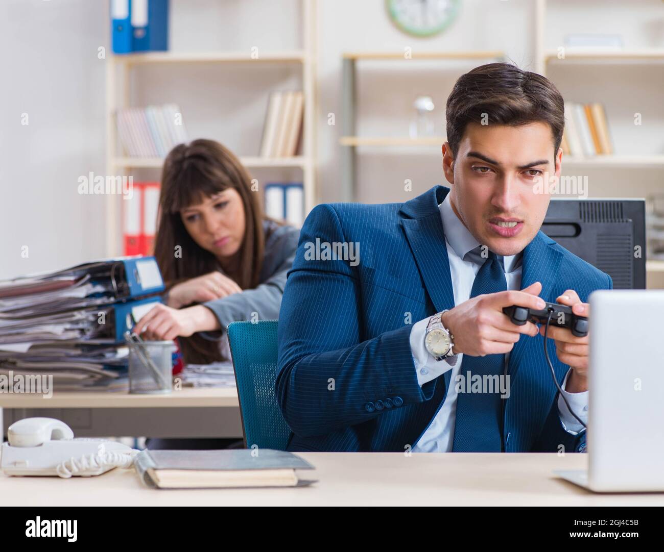 The man playing games in office while colleague is busy Stock Photo - Alamy