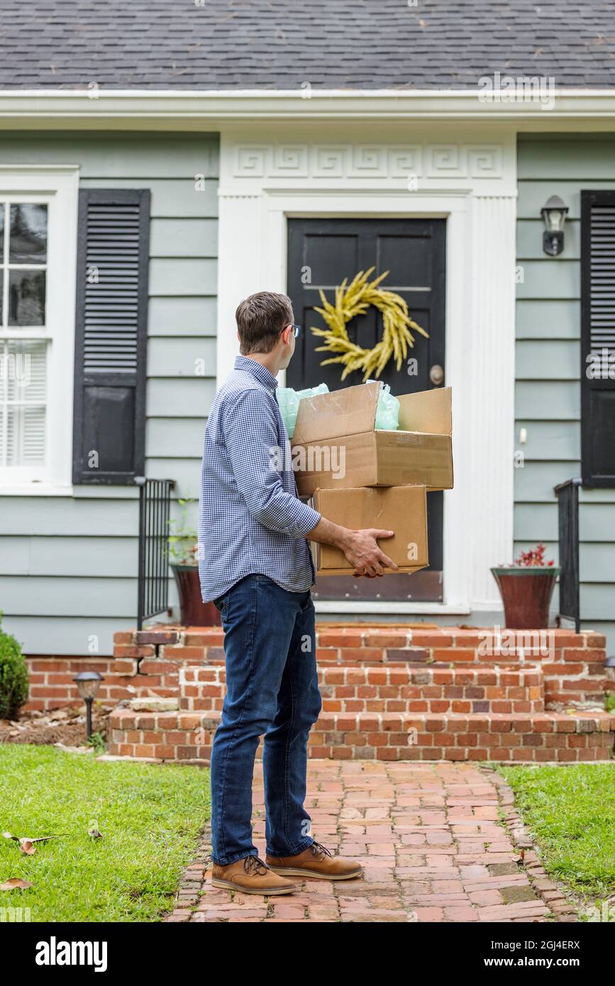 A man and father holding moving boxes outside a small blue cottage ...