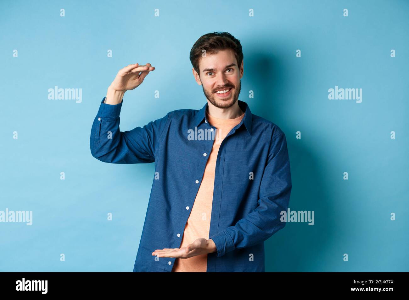 Handsome caucasian guy showing something big, shaping large size object ...
