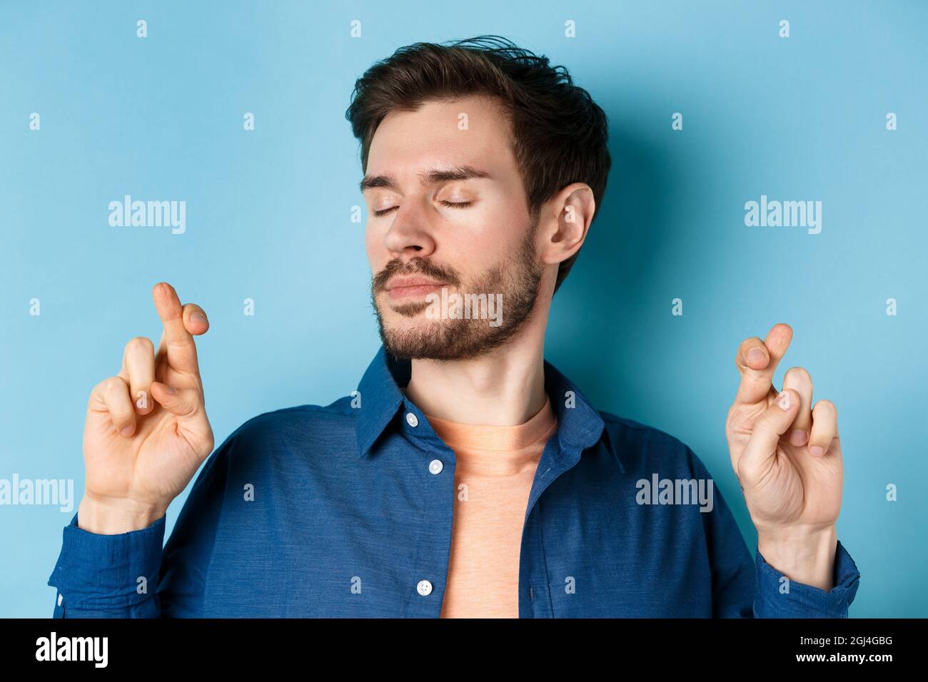 Close up of hopeful young man cross fingers for good luck and close ...