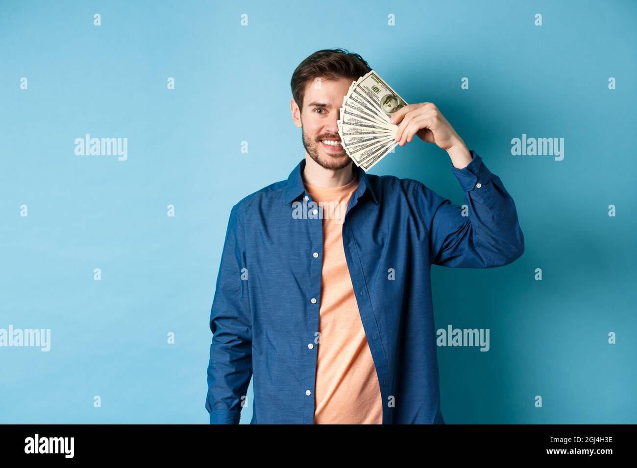 Happy young guy covering half of face with dollars and smiling, winning ...