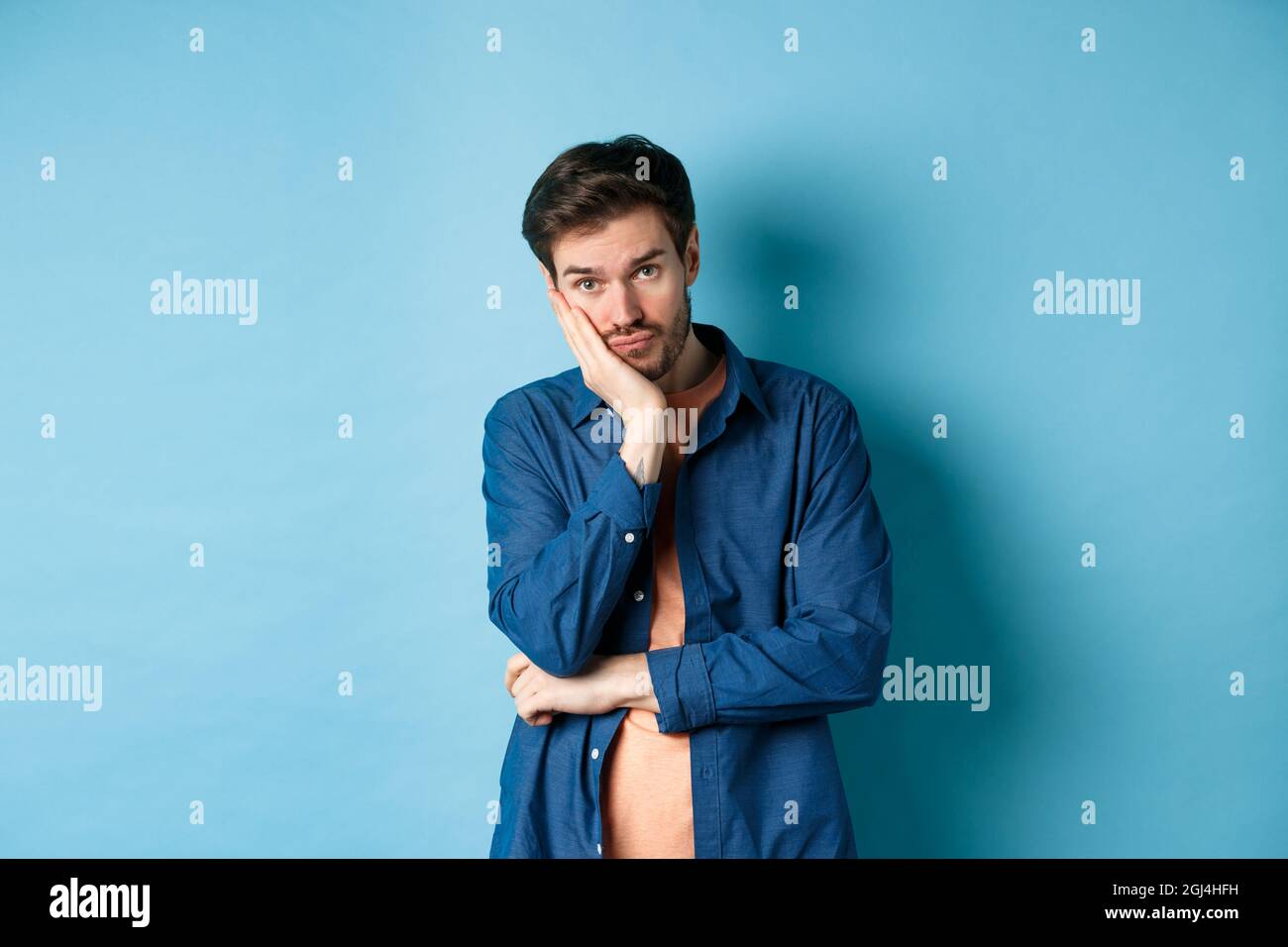 Sad and bored man lean face on hand, looking at camera empty-headed ...