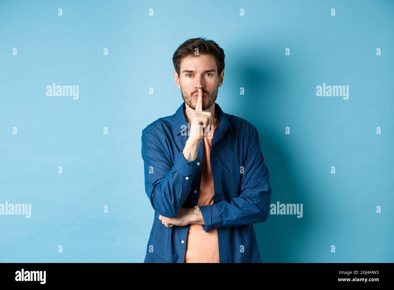 Modern guy shushing at camera, press finger to lips and telling a ...