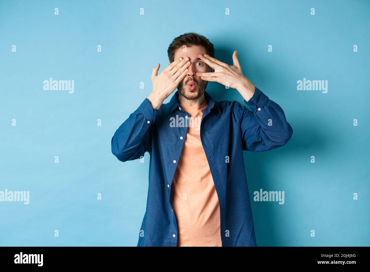 Excited young man peeking through fingers and saying wow, checking out ...