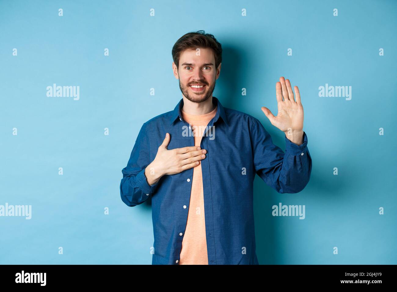 Honest young man smiling and making promise, holding hand on heart and ...
