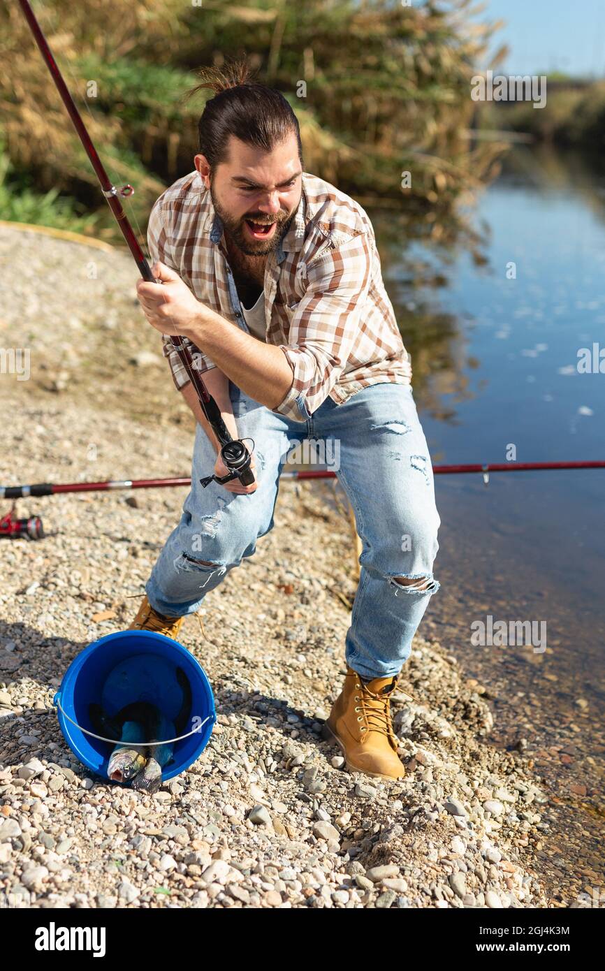 Adult man standing near river and pulling fish expressing emotions of ...