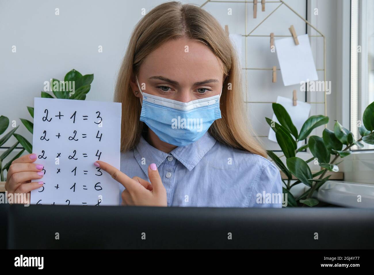Young female teacher wearing medical face mask sitting at desk and ...