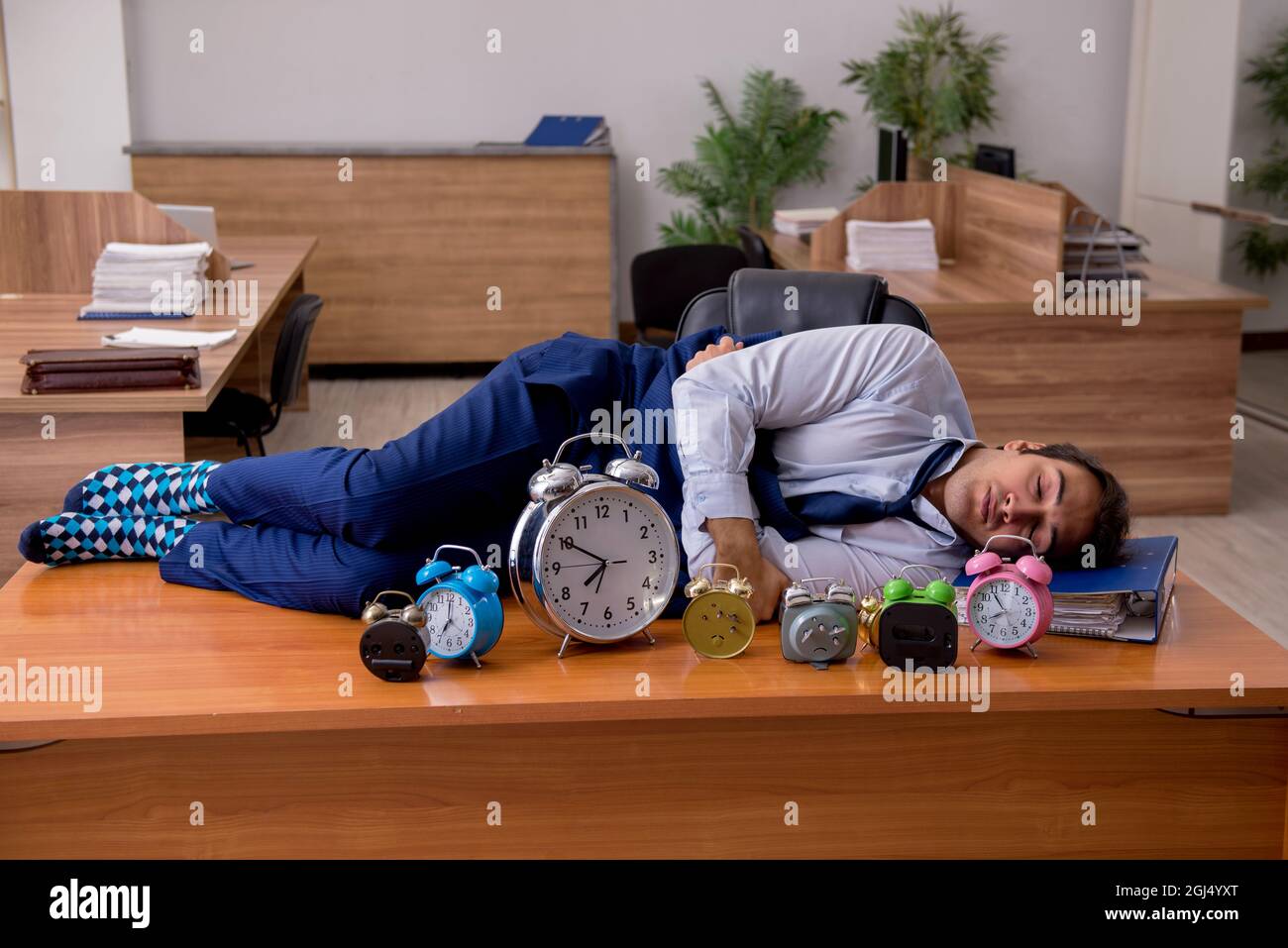 Young businessman sleeping in the office in time management concept ...