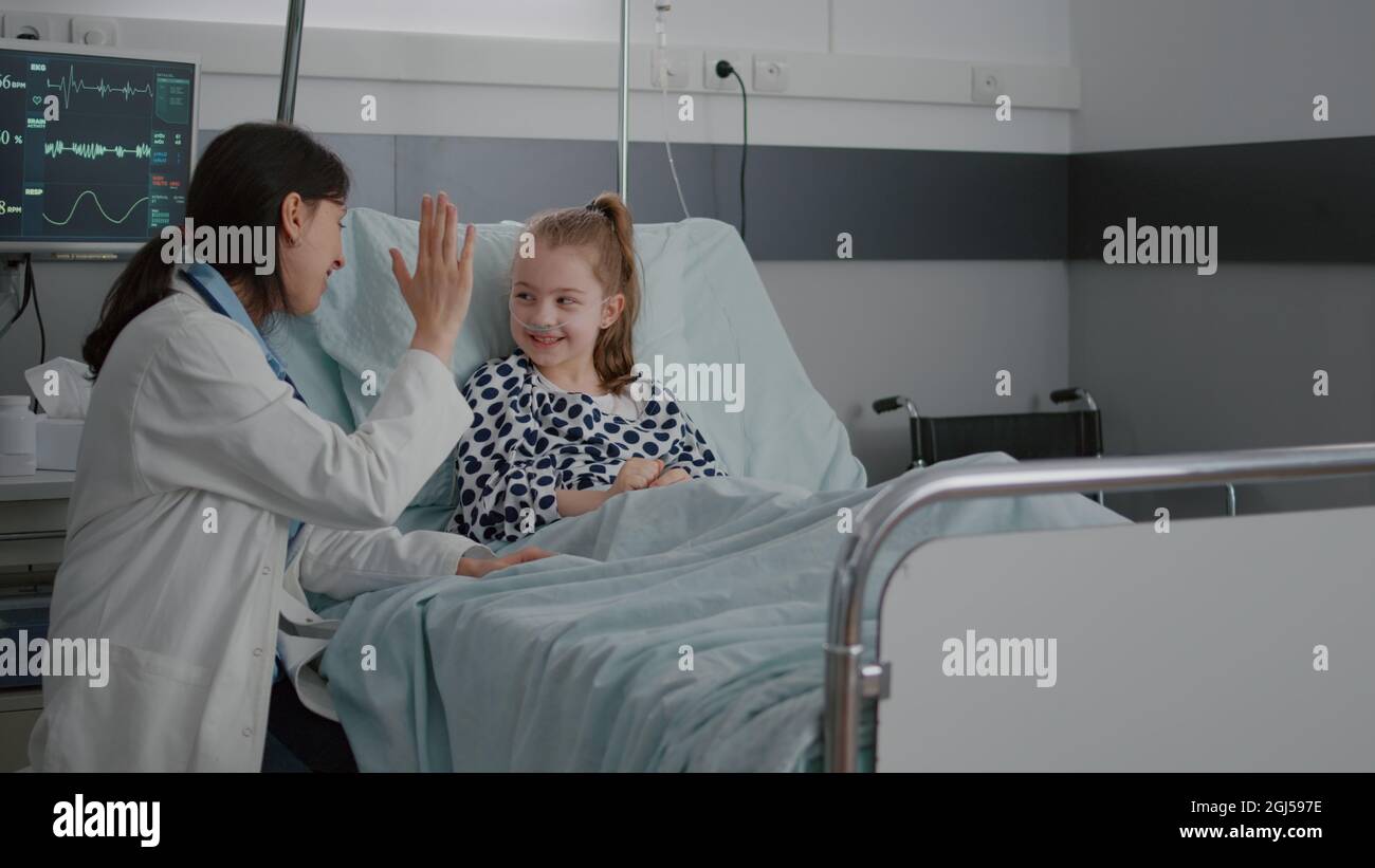 Pediatric woman doctor interacting with sick patient giving high five ...