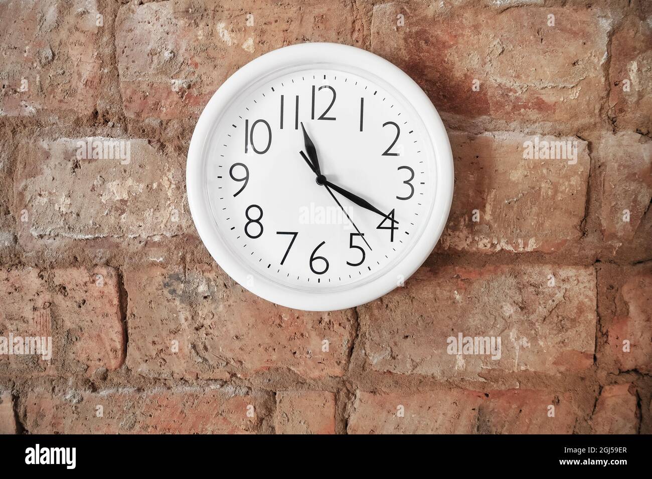 White classic clock on red brick wall. Twenty minutes past eleven Stock ...