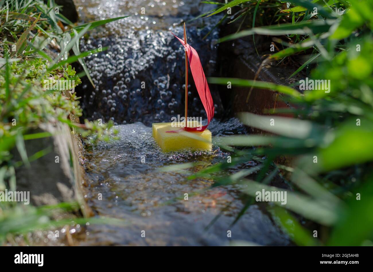 A yellow children's boat with a red sail into a narrow channel o Stock ...