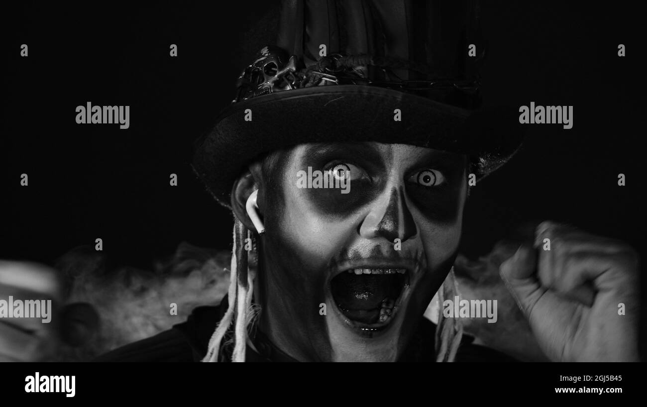 Creepy man with skeleton makeup in top-hat. Guy wearing earphones, listening music, dancing ...