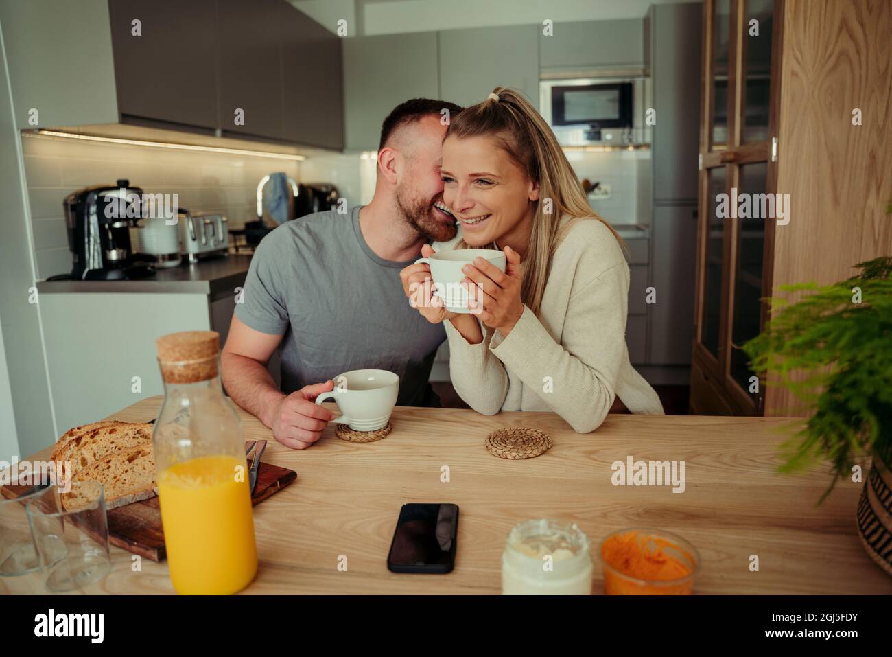 Caucasian happy couple sitting at kitchen table whispering in ear Stock ...