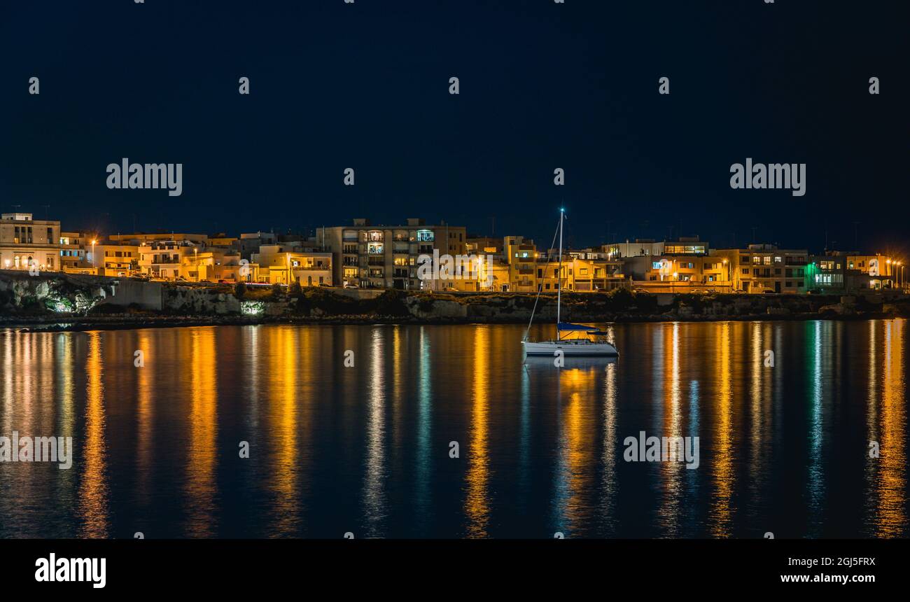 Waterfront with city lights reflection on water with a sailboat at ...