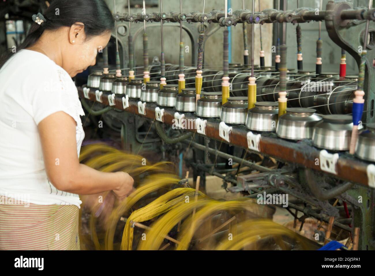 Woman working at machine making cotton threads on spools in fabric ...