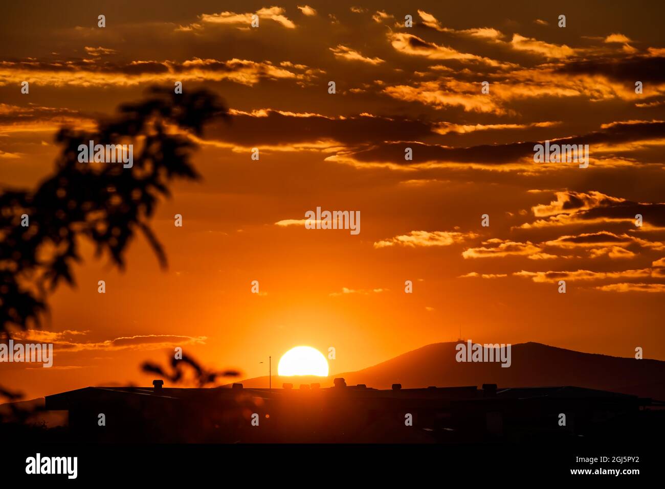 Fiery sunset over rooftops and far away hills in the summer time. Soft ...