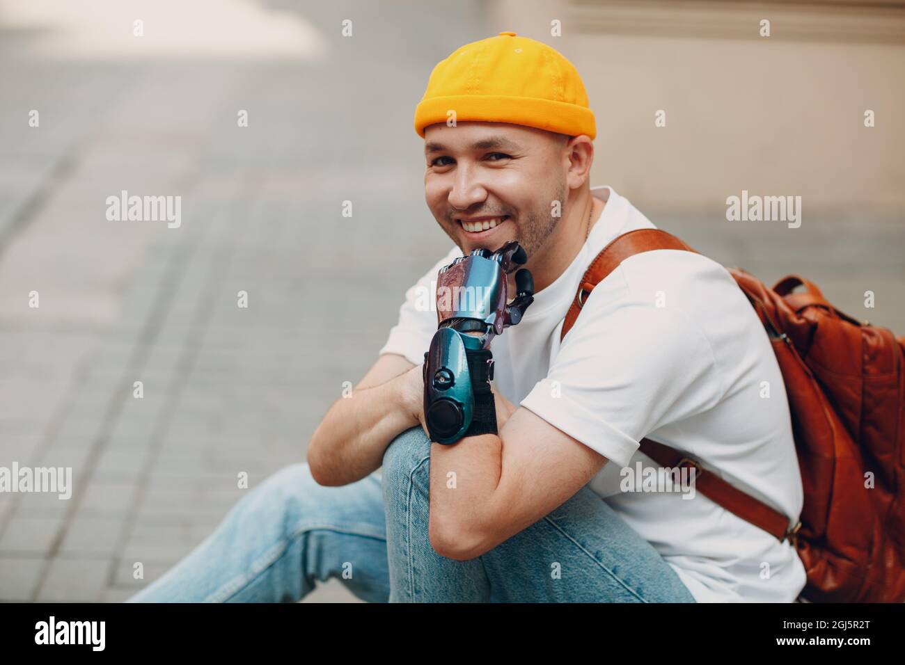 Young disabled man with artificial prosthetic hand sitting on sidewalk ...