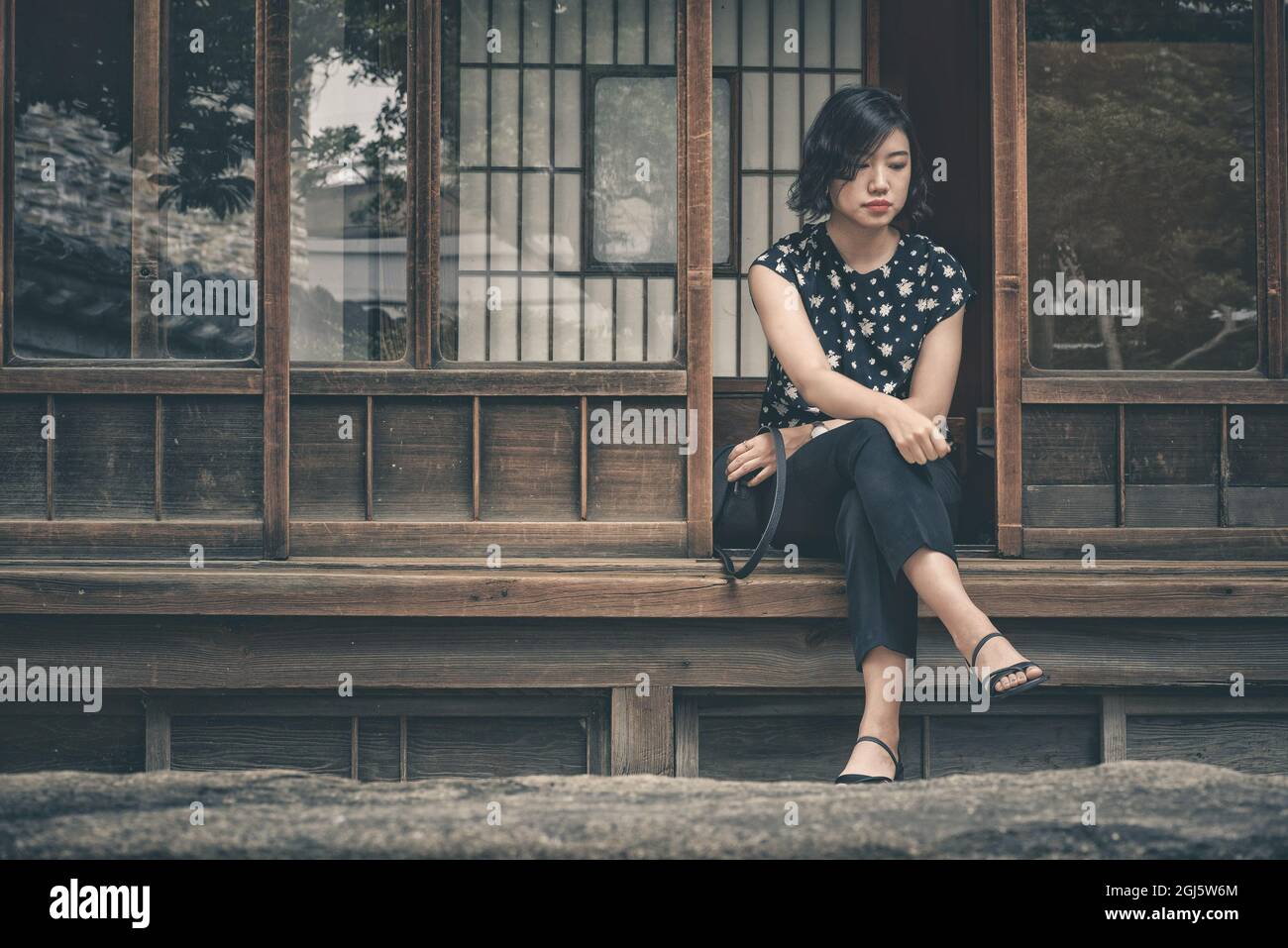Sad East Asian girl sitting on a wooden doorway and waiting for someone ...