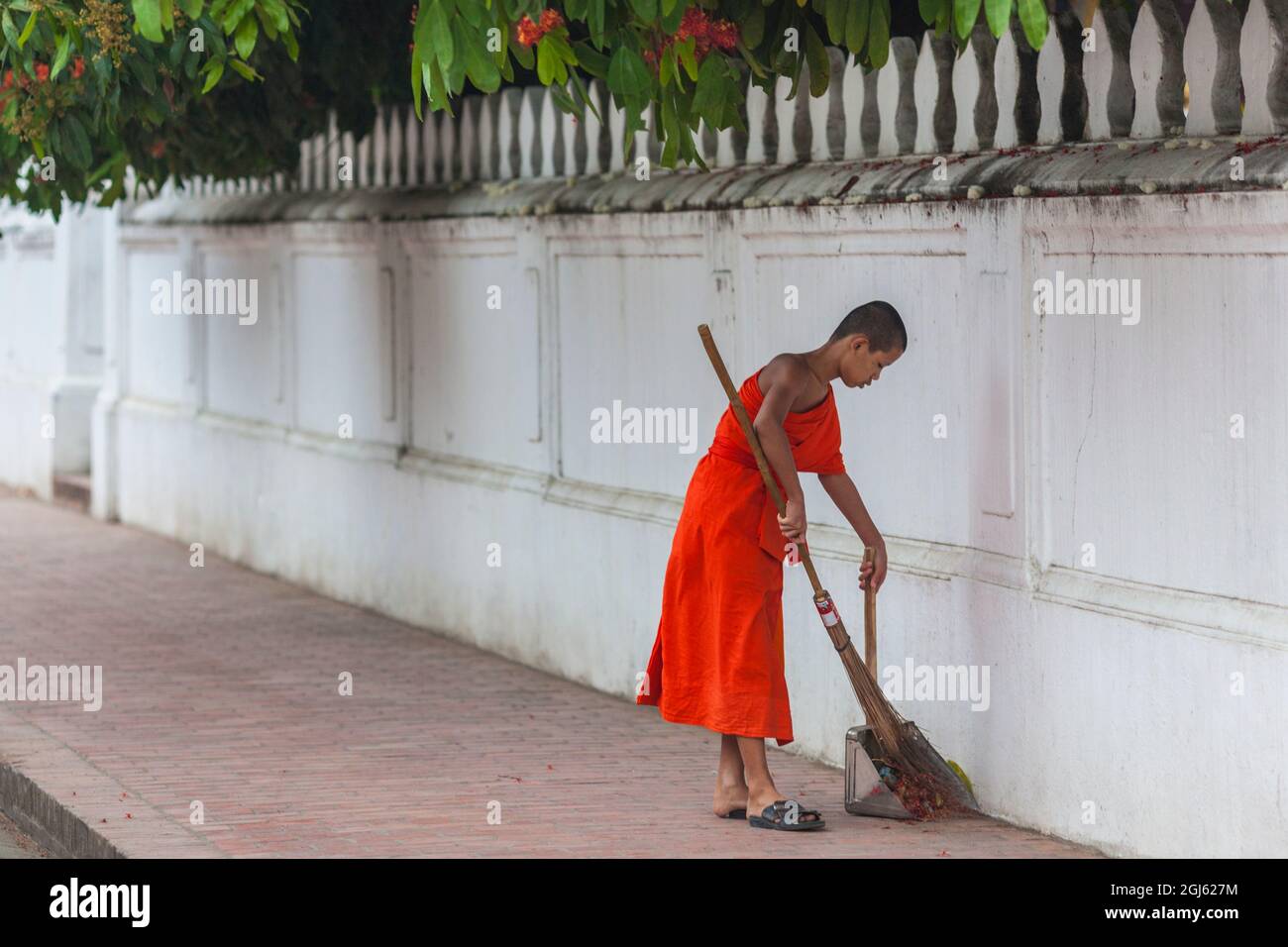 Laos, Luang Prabang. Sisavangvong Road, young Buddhist monk sweeping ...