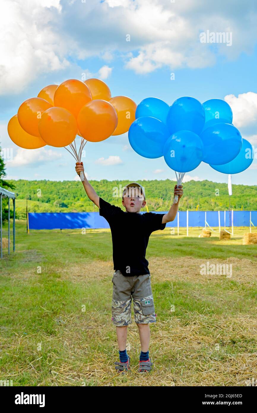 Boy jumping holding a bunch of balloons, orange and blue Stock Photo ...