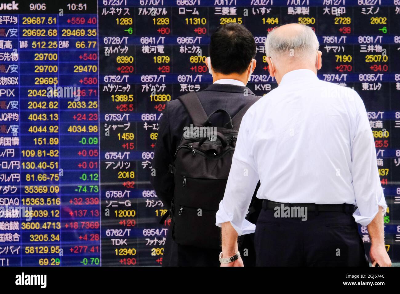 Japanese business men walk towards an ic board showing stock market ...