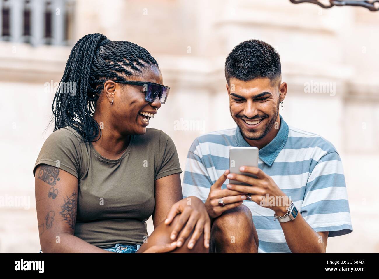 Black Woman Sitting Next To A Man Laughing While Looking At The Mobile