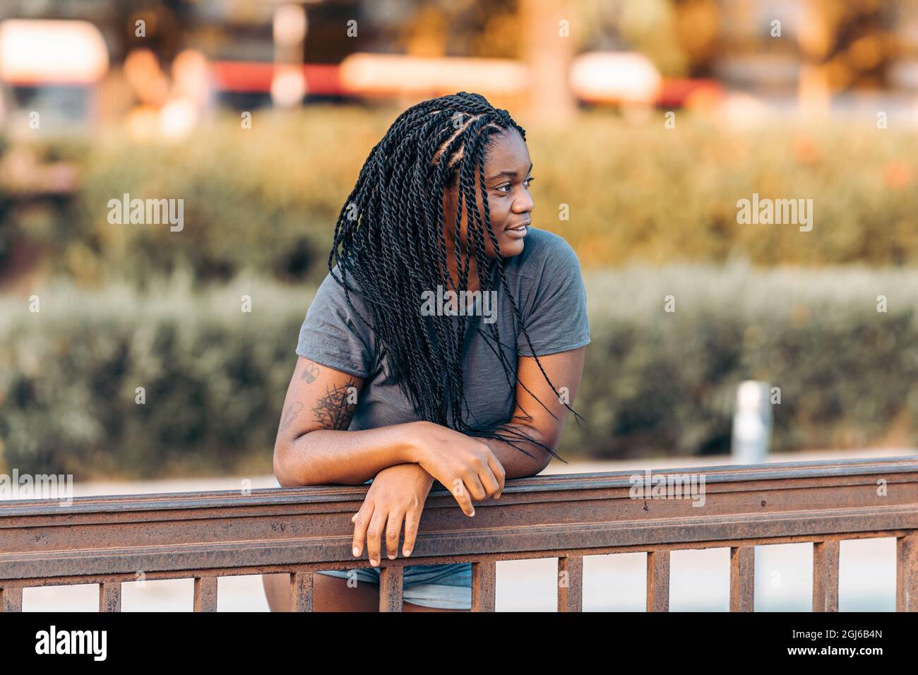 Distracted afro woman with braided hair leaning on a rail in the street ...