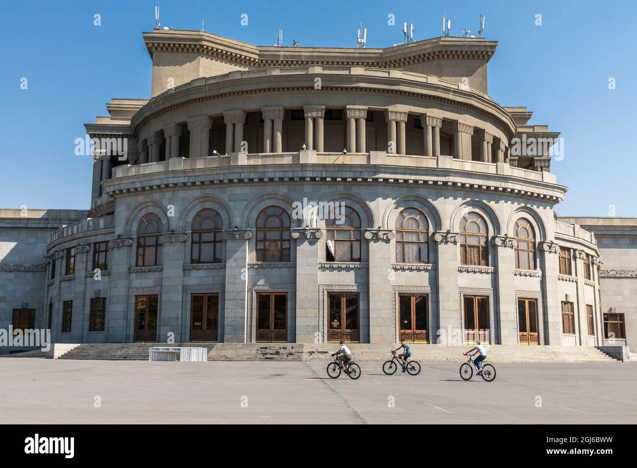 Armenia. Yerevan. Three boys ride bicycles past the Armenian Opera ...