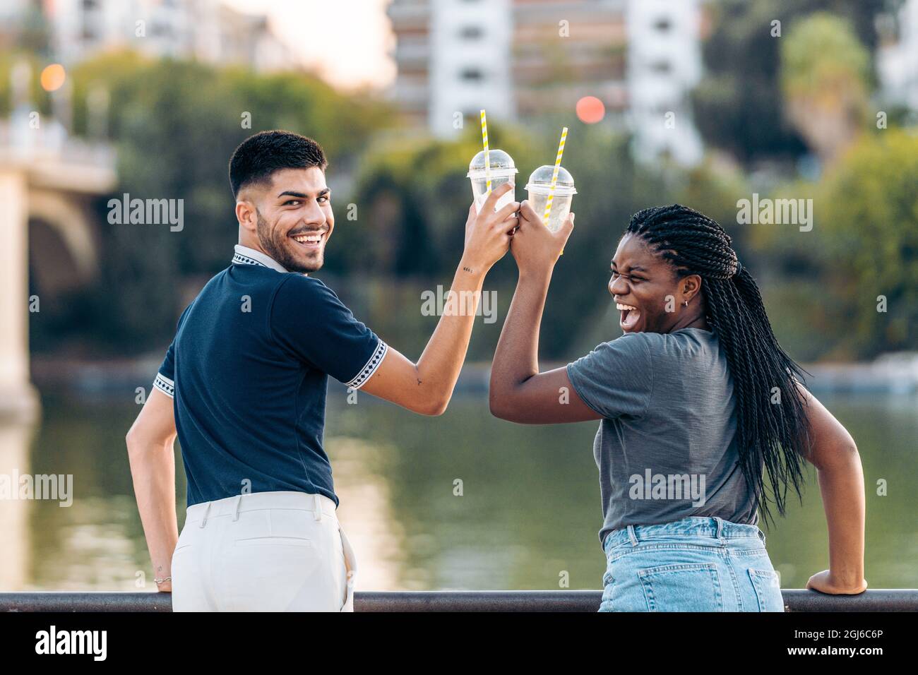 Two multiethnic people toasting with a shake while laugh outdoors Stock ...