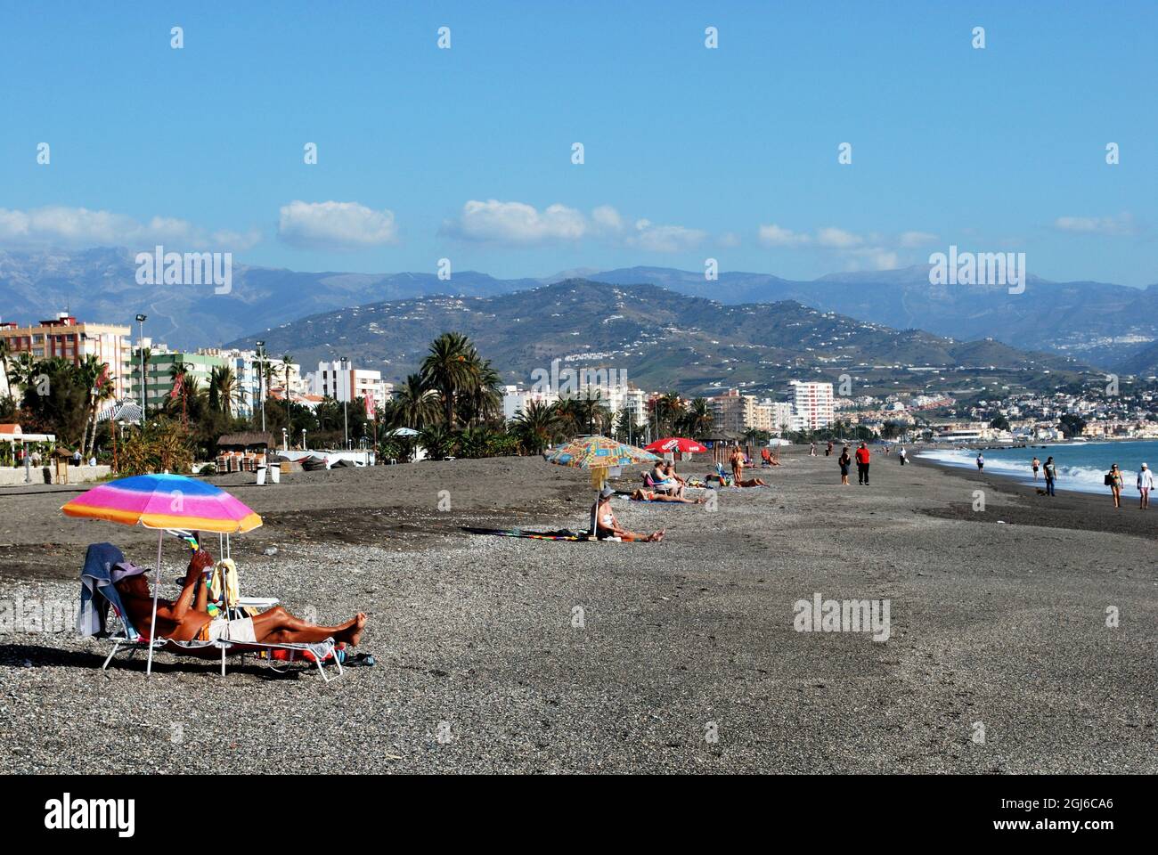 View along the beach with mountains to the rear and tourists sunbathing ...