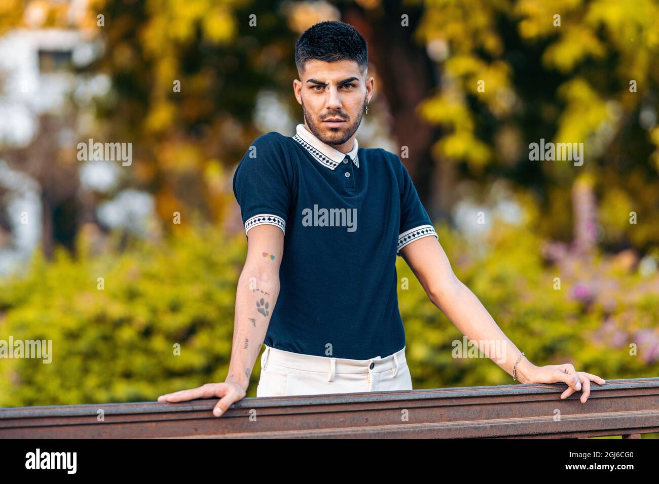 Portrait if a man with modern clothes and tattoos leaning on a rail in ...