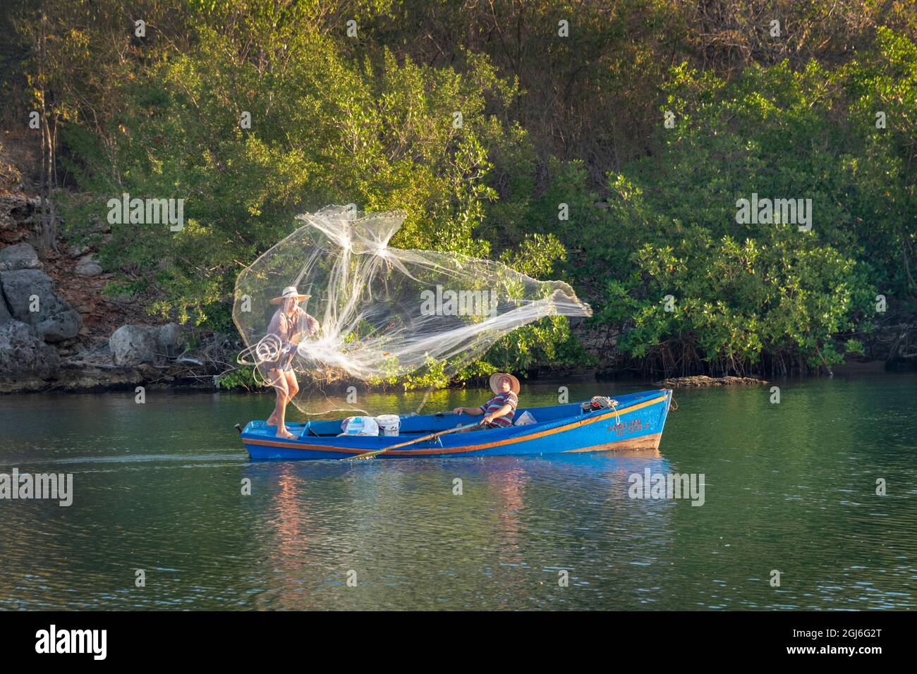 Early morning fisherman casts net from wooden row boat on Rio Guaurabo ...
