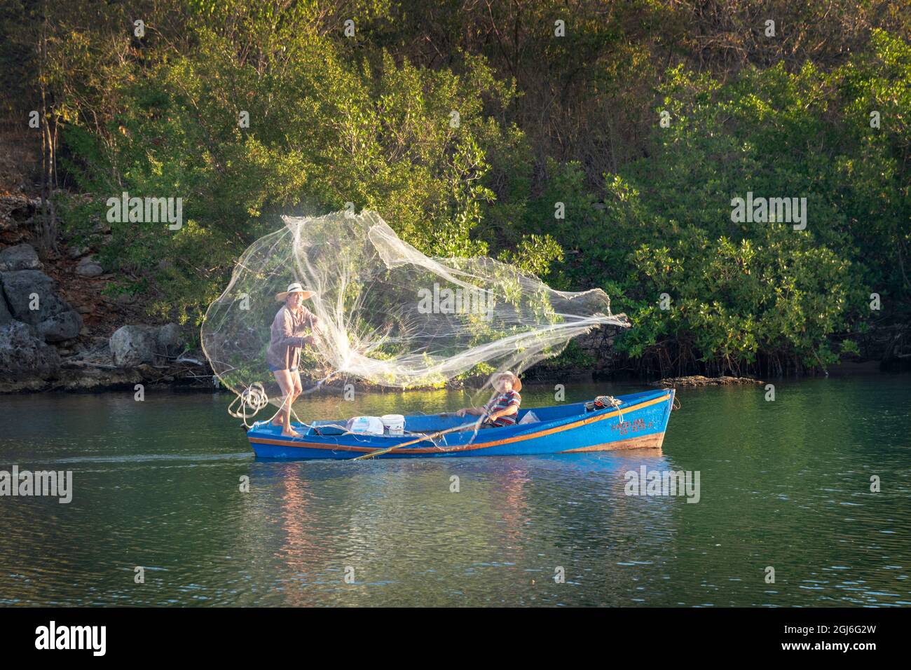Early morning fisherman casts net from wooden row boat on Rio Guaurabo ...