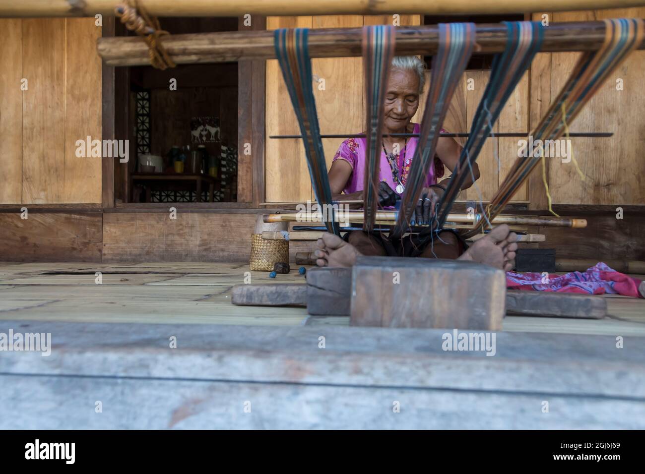 Senior woman with indigo stained hands weaving an ikat cloth in the ...